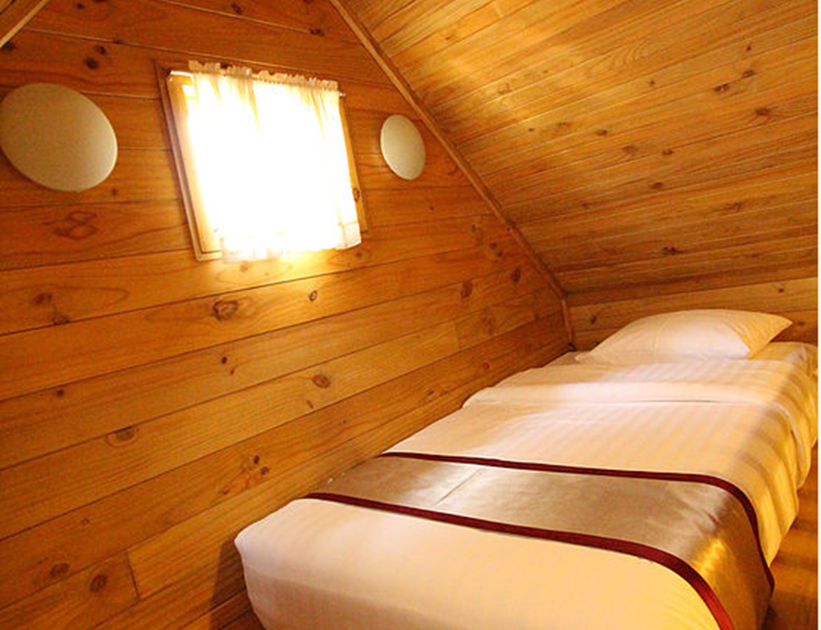 Uma cama de solteiro num quarto de cabana de madeira, com teto inclinado e duas decorações redondas nas paredes.