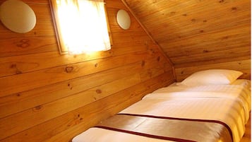 Uma cama de solteiro num quarto de cabana de madeira, com teto inclinado e duas decorações redondas nas paredes.