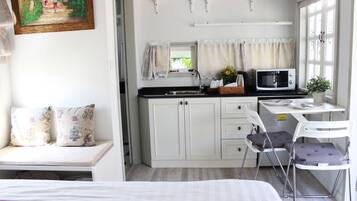 Quarto compacto com cama, pequeno espaço de cozinha, área de refeições e janela com cortinas.