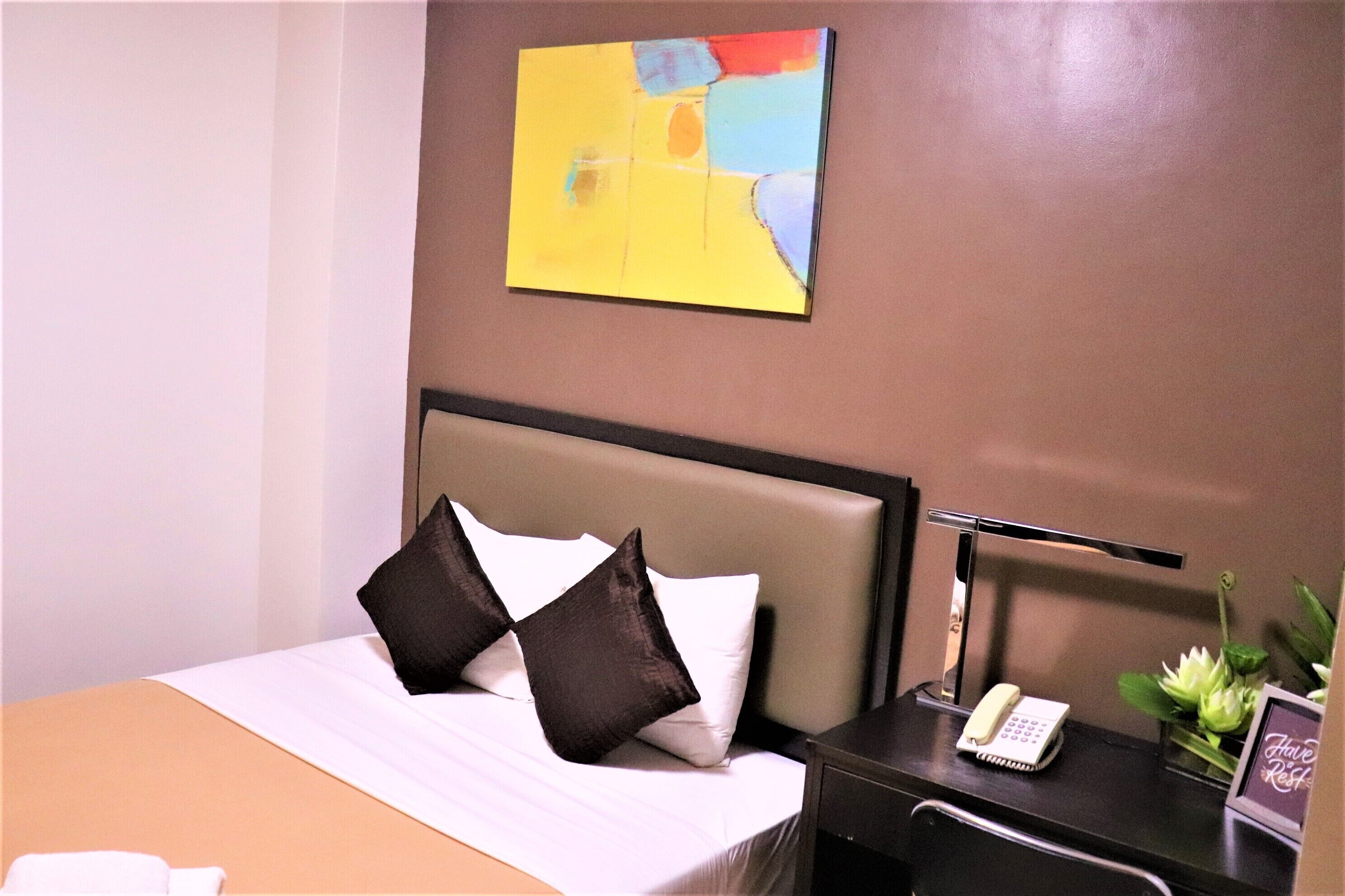 Quarto de hotel com uma cama, mesa de cabeceira com abajur, telefone e uma pequena planta.