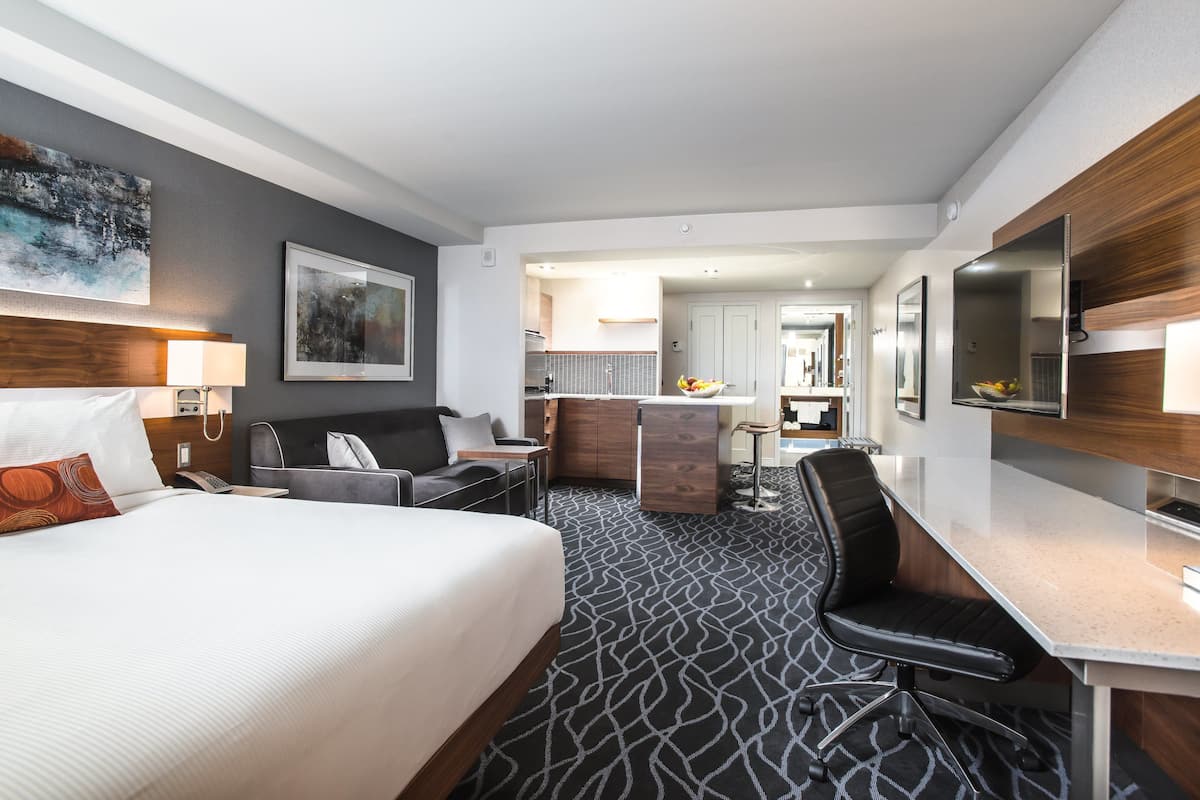 Quarto de hotel com cama, escrivaninha e cozinha compacta.