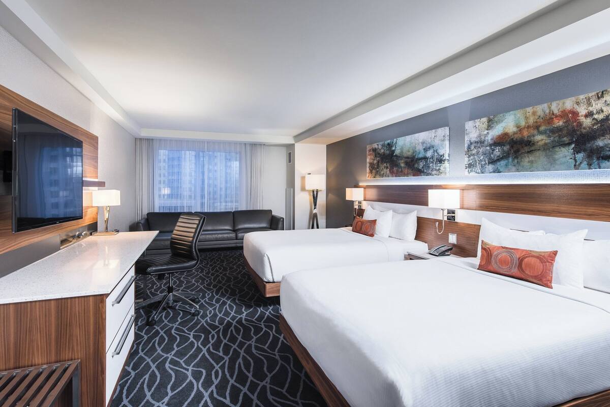 Quarto de hotel com uma cama grande, uma escrivaninha, uma televisão e um quadro na parede.