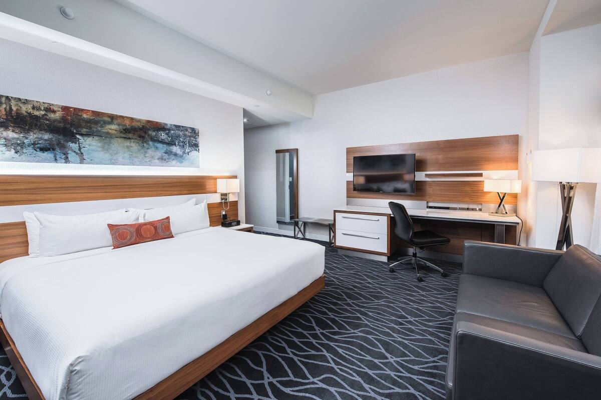 Quarto de hotel com uma cama grande, uma escrivaninha, uma televisão e um sofá.