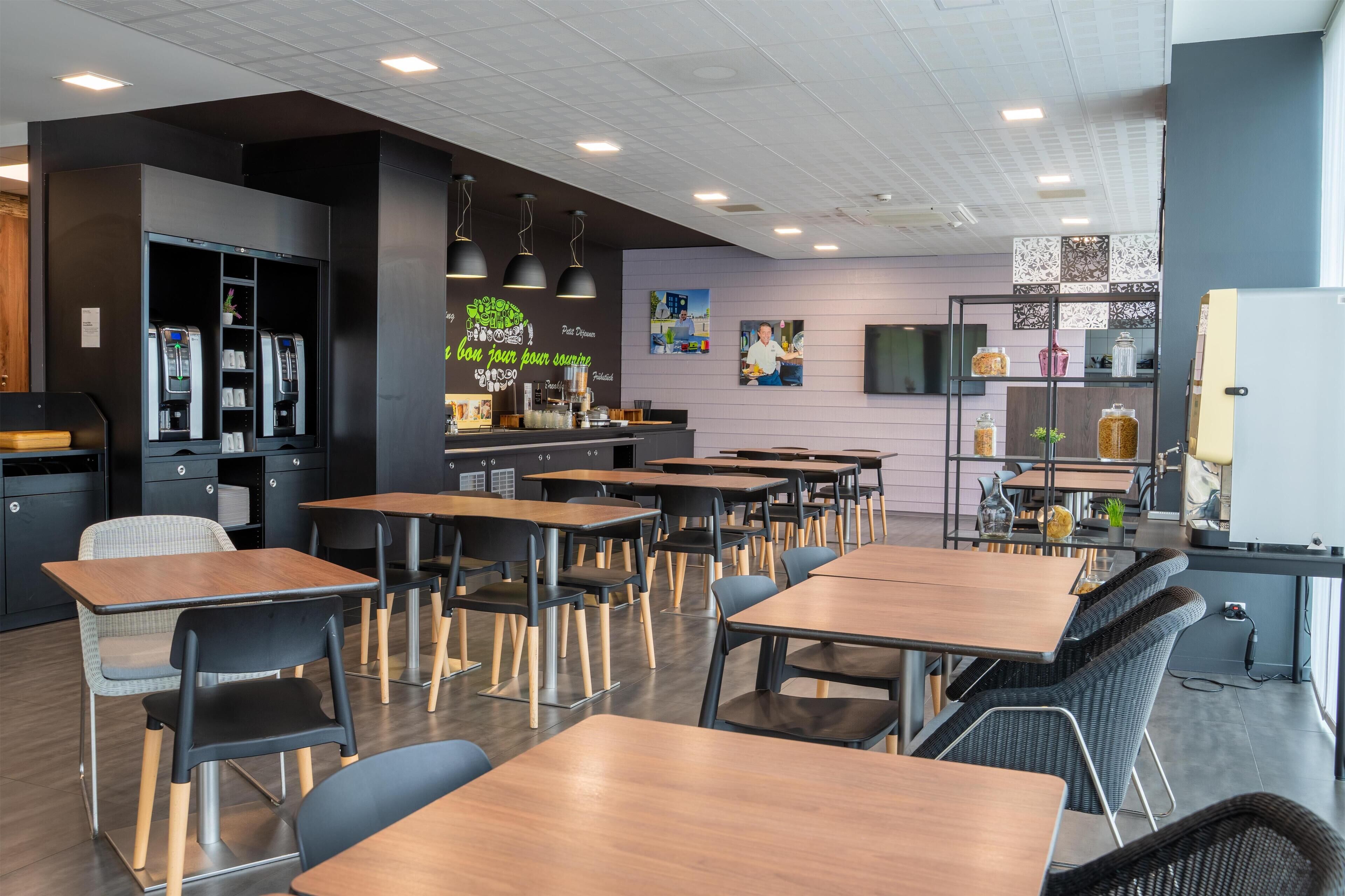 Um café moderno com mesas de madeira e cadeiras pretas, uma máquina de café e um quadro de menu na parede.