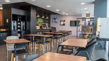 Um café moderno com mesas de madeira e cadeiras pretas, uma máquina de café e um quadro de menu na parede.