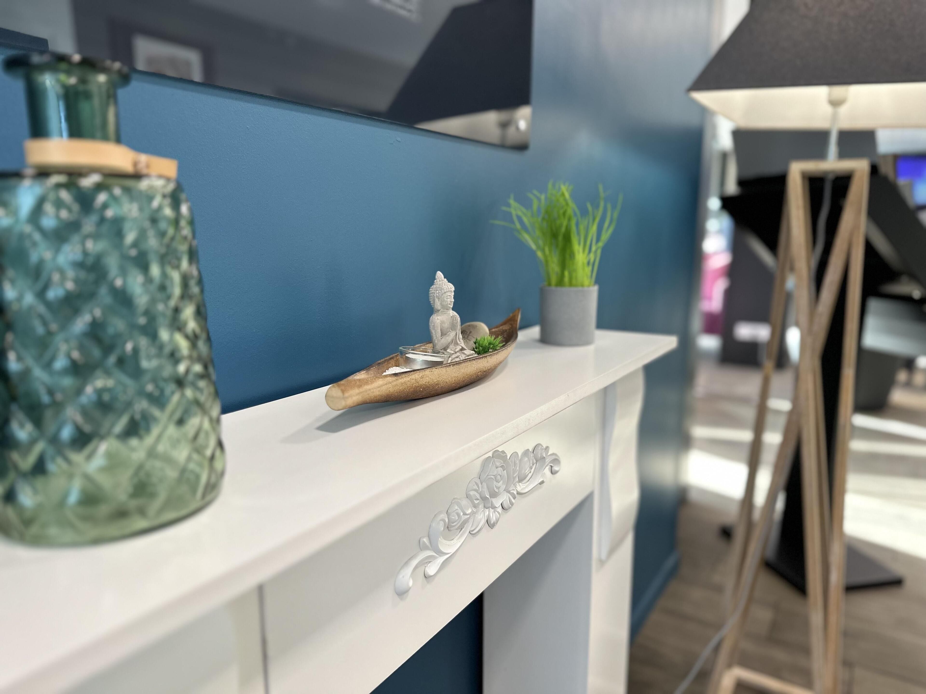 Um console branco com uma estátua de Buda, uma pequena planta em vaso e uma tigela decorativa.