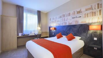 Quarto de hotel com uma cama grande, uma escrivaninha com cadeira, um guarda-roupa e uma parede com quadros.