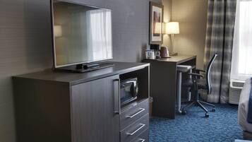 Quarto de hotel com televisão de tela plana, escrivaninha com luminária, cadeira, micro-ondas e cama.