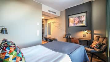 Quarto de hotel com cama, escrivaninha, cadeira e televisão.