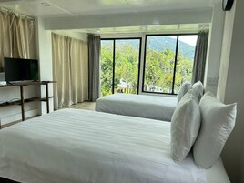Quarto de hotel com duas camas, televisão sobre um suporte e janelas amplas com vista para as montanhas.