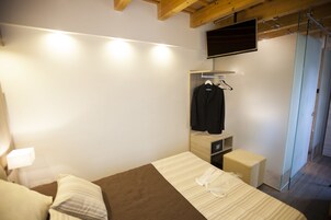Quarto com cama, mesa de cabeceira, abajur e cabideiro.