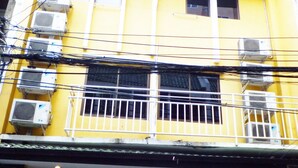 Um edifício de dois andares com várias unidades de ar condicionado, uma varanda e plantas em vasos na frente.