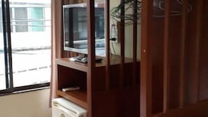 Quarto compacto com cozinha compacta, mini-geladeira, armário de madeira com televisão e janela com vista para um edifício.