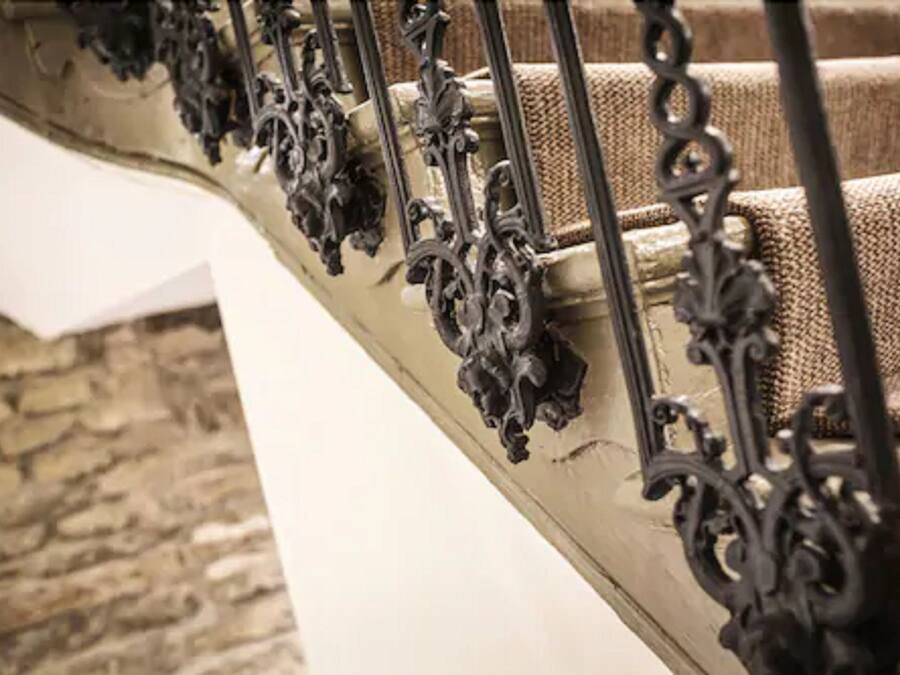 Escadaria com guarda-corpo de metal preto ricamente decorado e parede de pedra.