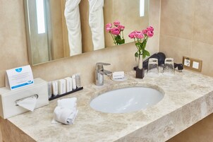 Um banheiro com pia de mármore, espelho, porta-toalhas, caixa de lenços e um vaso com flores.