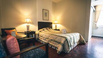 Quarto de hotel com cama, uma cadeira, mesa e duas luminárias.