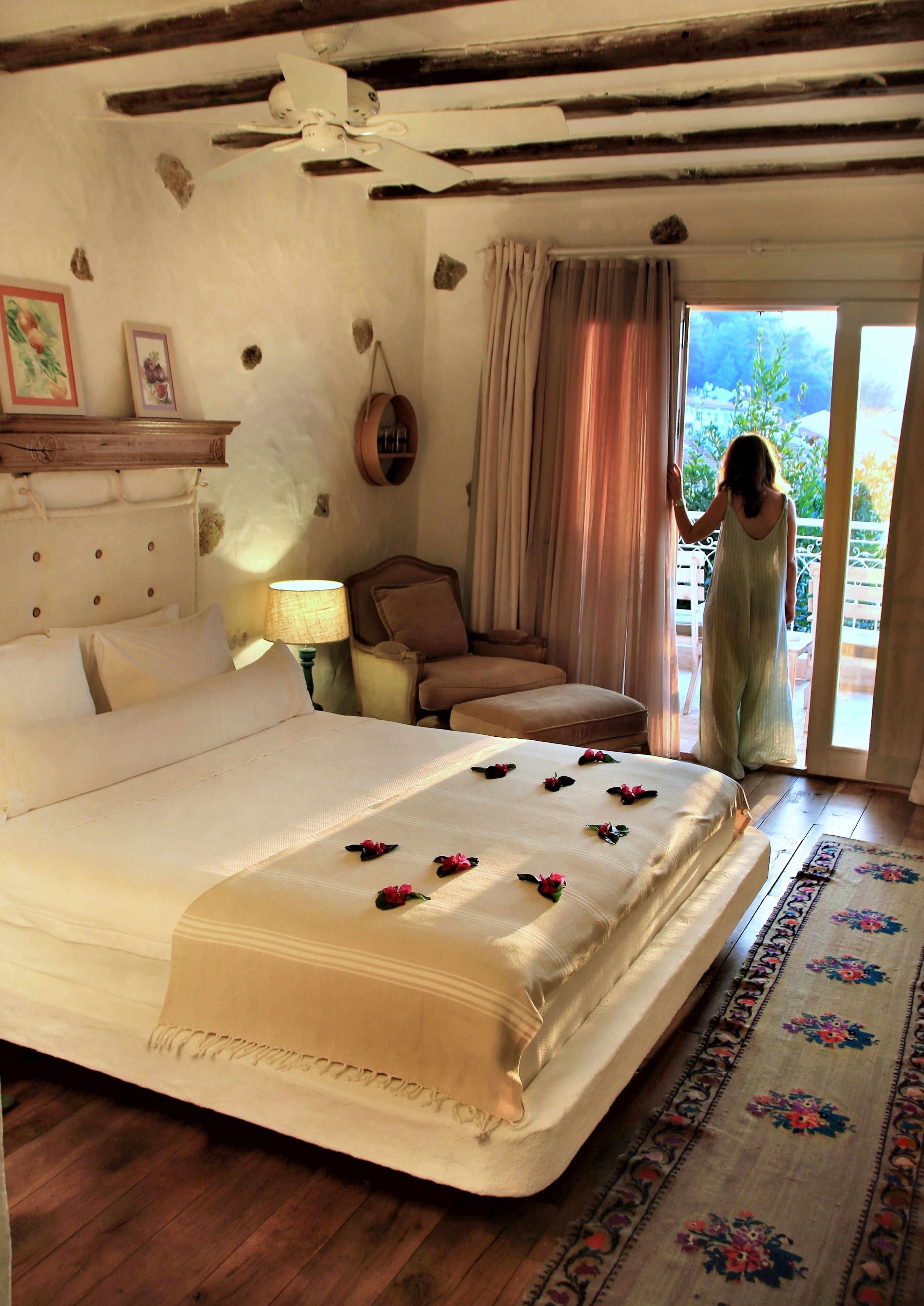 Quarto com uma cama grande, piso de madeira, ventilador de teto e vista para o exterior.