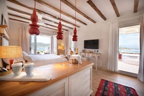Quarto de hotel com escrivaninha de madeira, duas mesas de cabeceira, uma cama, televisão e varanda com vista.