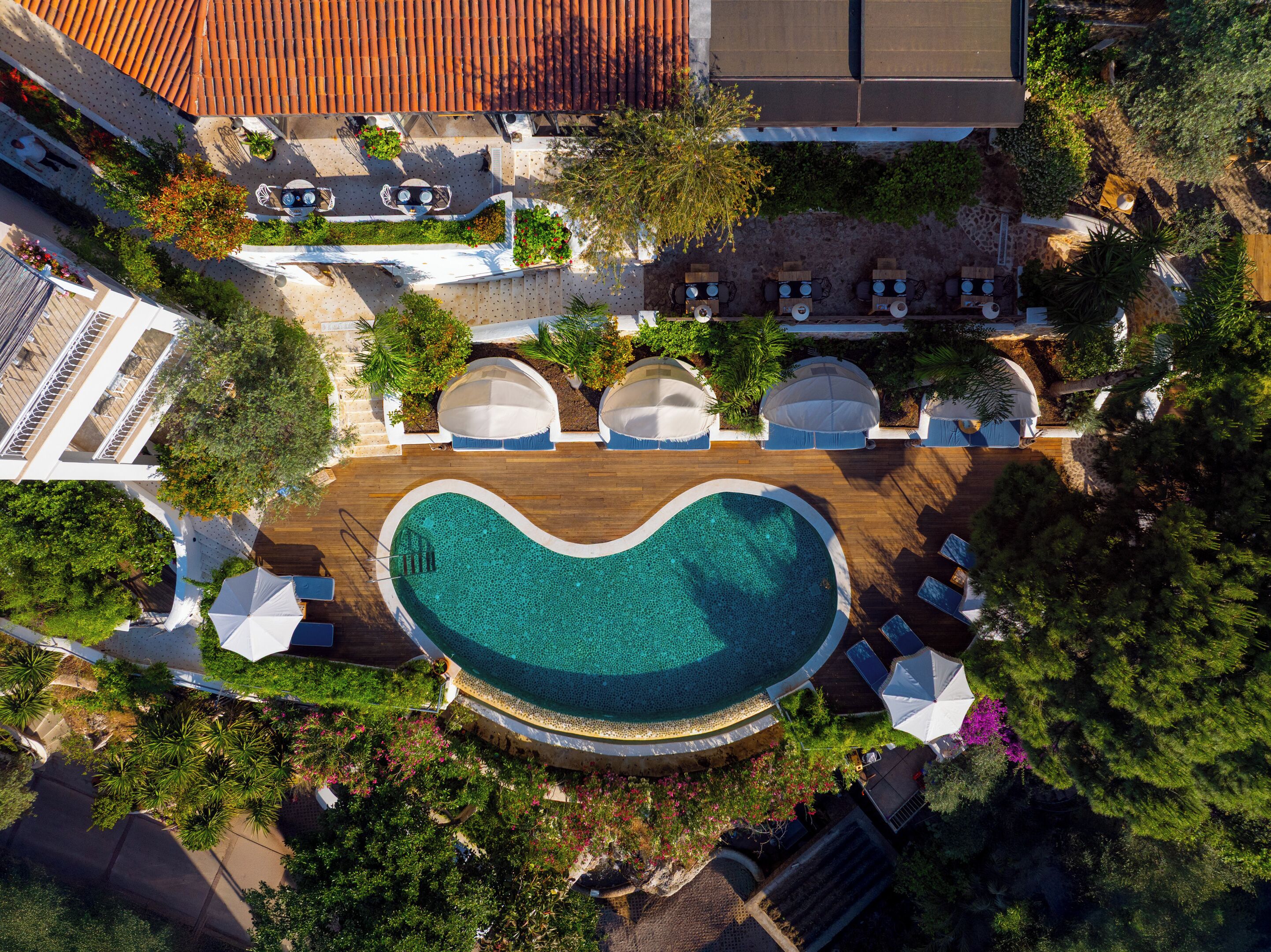 Vista aérea de um resort com piscina em formato de coração, áreas de estar e um espaço coberto com assentos.