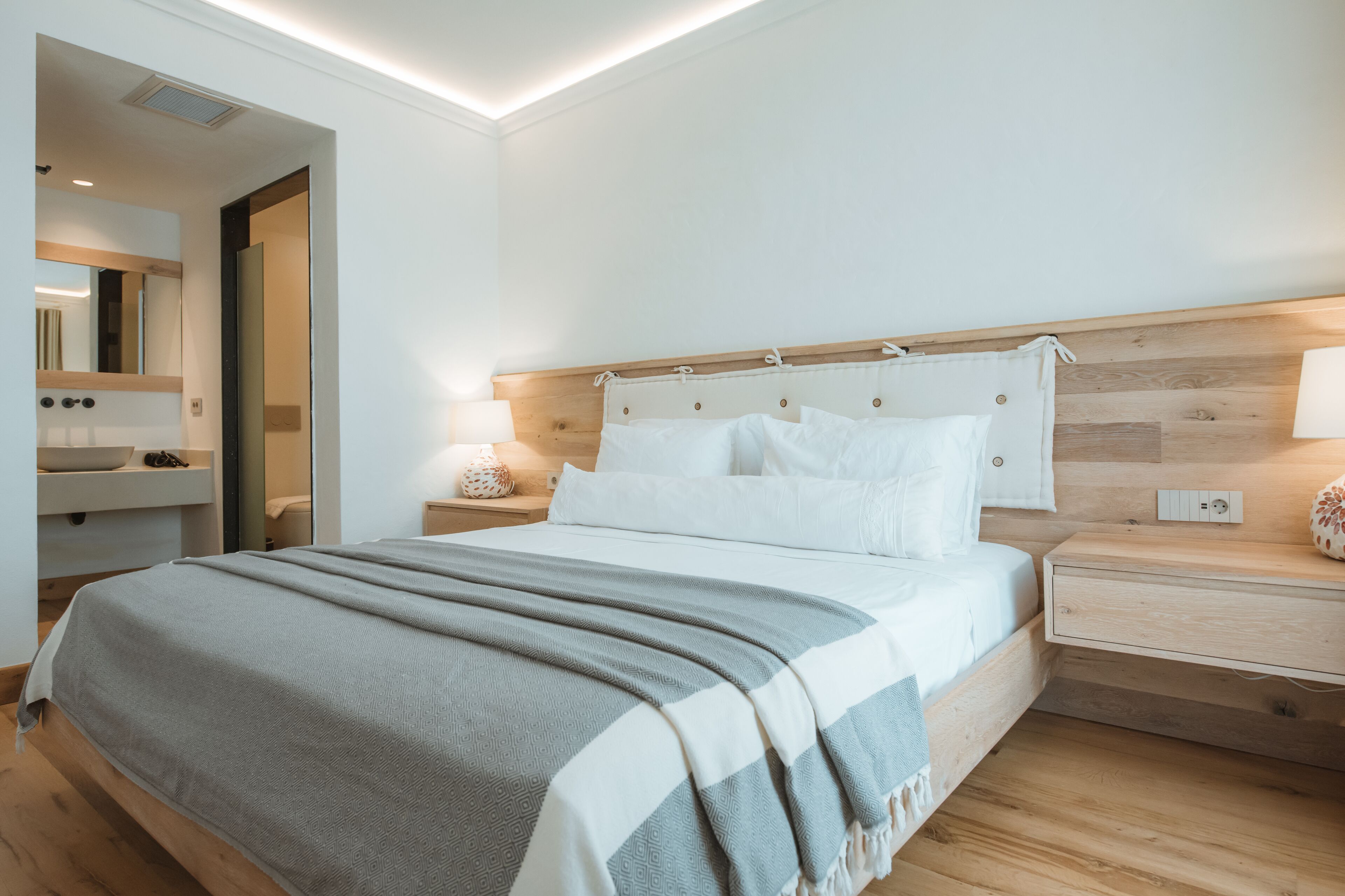 Quarto moderno com uma cama grande, mesas de cabeceira, um criado-mudo, um espelho e uma cabeceira de madeira.