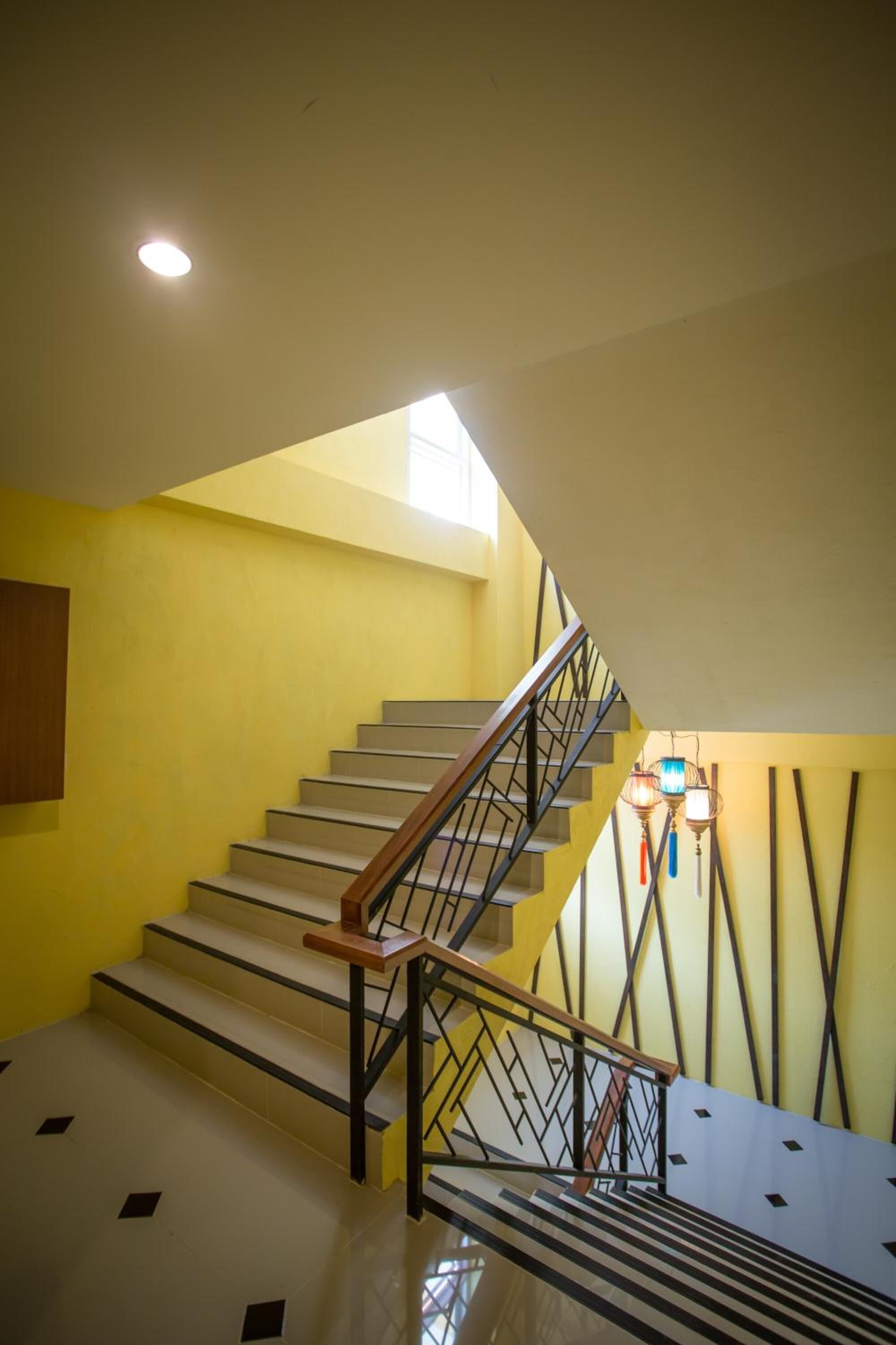 Uma escadaria com corrimãos de madeira e guarda-corpo de metal, que leva a um patamar com luminária decorativa.