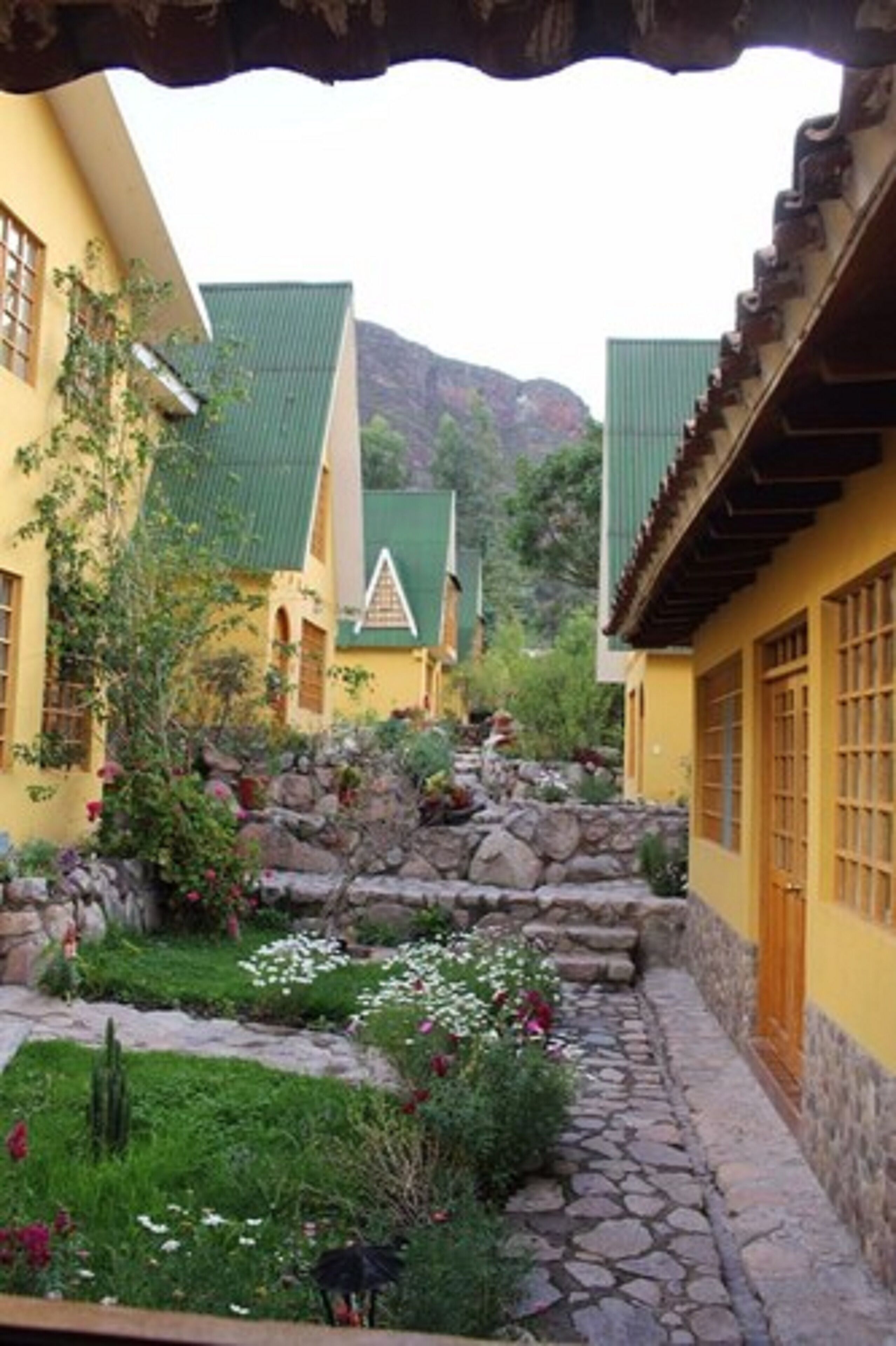 Um pátio com caminhos de pedra, um pequeno jardim com flores e edifícios tradicionais com telhados verdes.