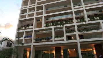 Um hotel com vários andares, um pátio central, um pequeno espelho d'água e varandas com plantas.