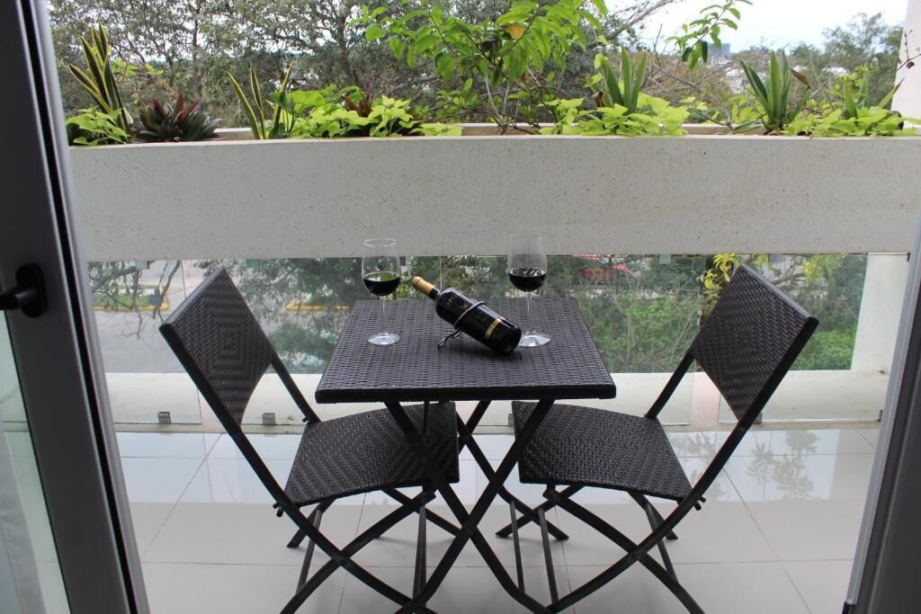 Varanda envidraçada com mesa, cadeiras, dois copos de vinho e uma garrafa.