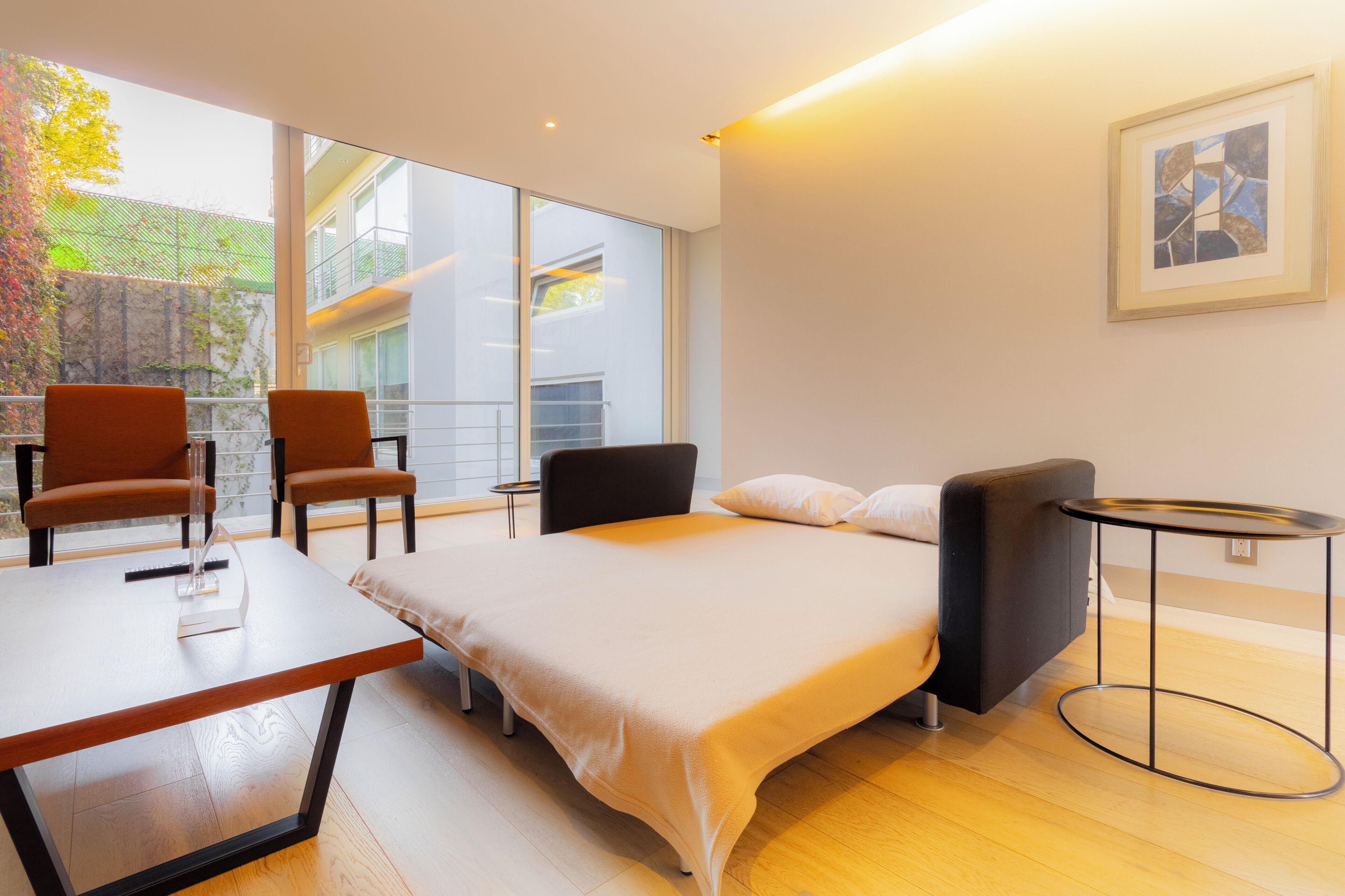 Quarto de hotel moderno com cama, duas cadeiras, uma mesinha e um apoio de mesa redondo.