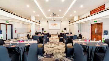 Uma sala de conferências com mesas redondas, cadeiras e uma tela de projetor exibindo 'HARRIS Seminyak Bali'.