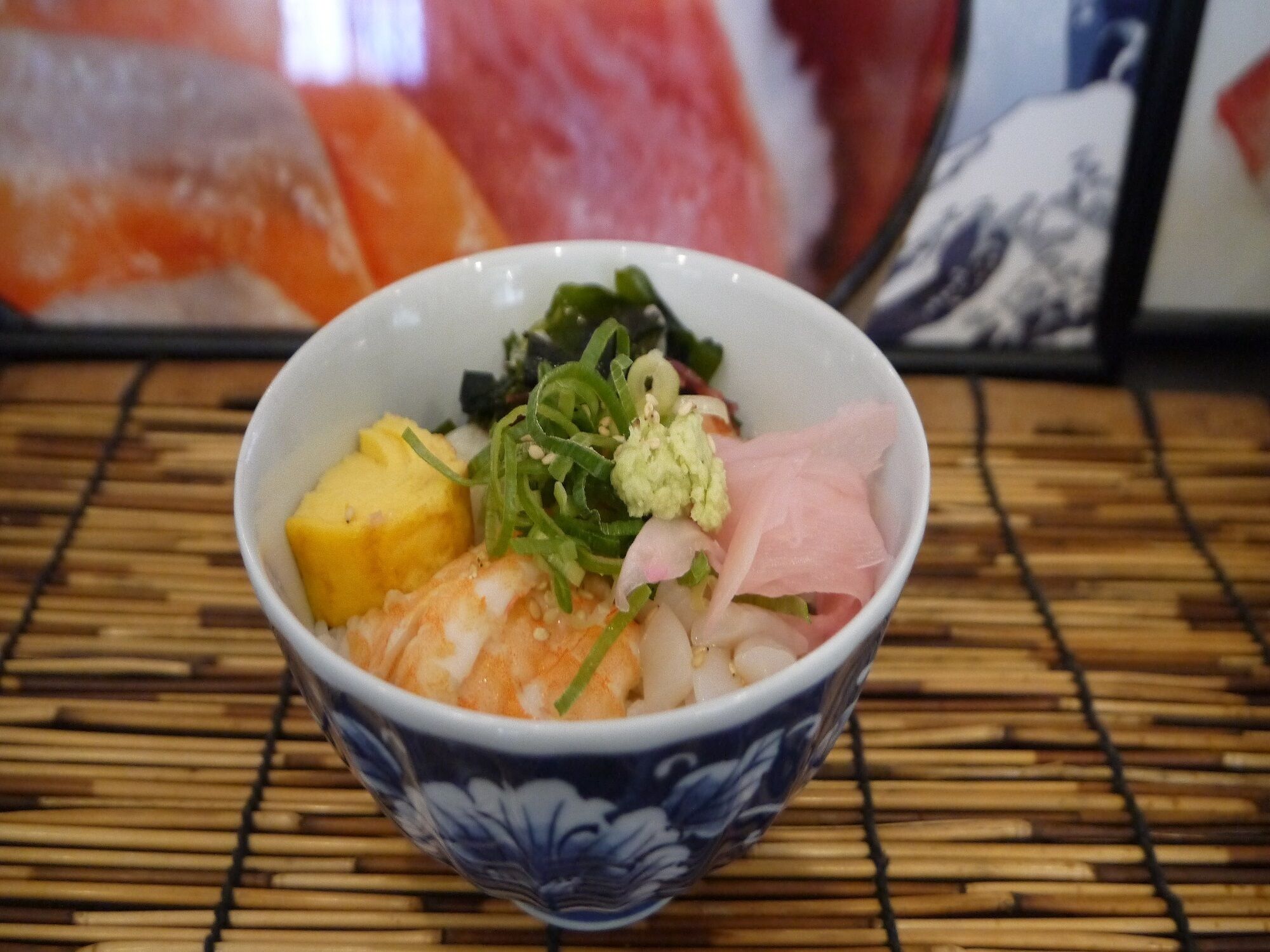 Uma tigela de comida com vários ingredientes sobre um tapete de bambu.