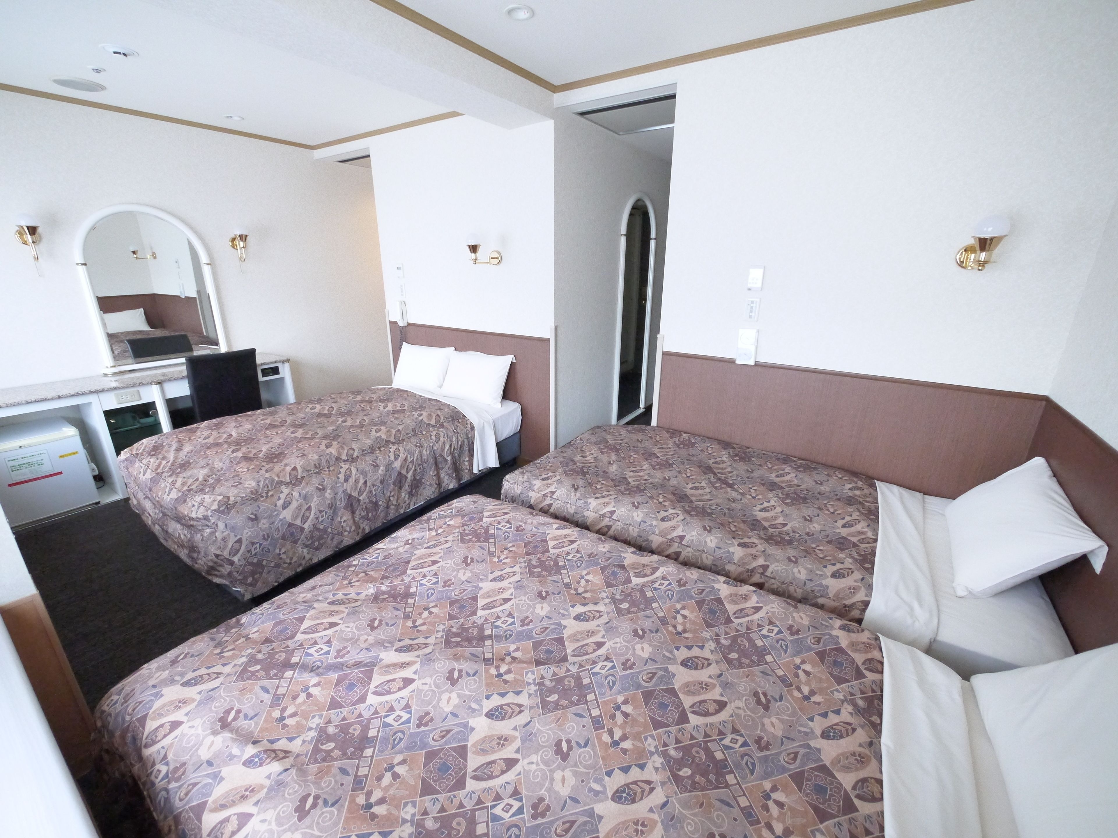 Quarto de hotel com duas camas, uma escrivaninha, uma cadeira, um espelho e um guarda-roupa.