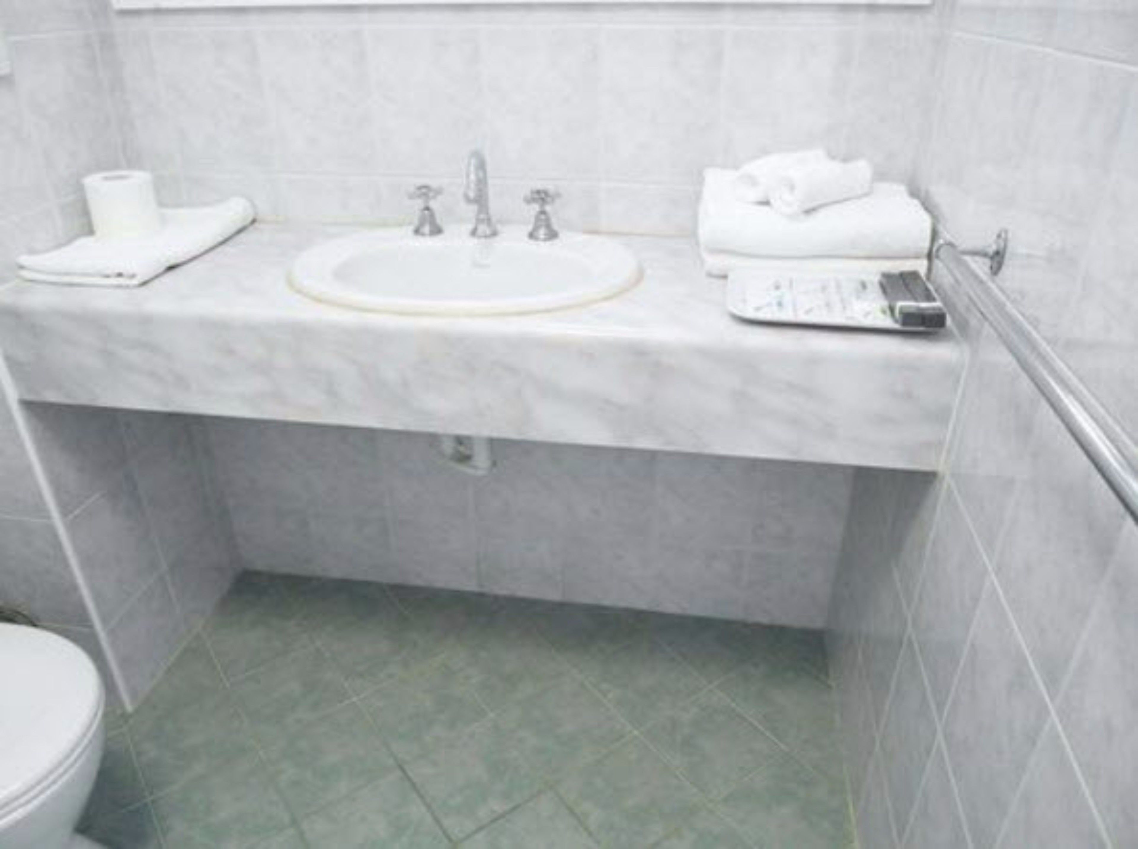Uma casa de banho com uma pia branca, duas torneiras, uma sanita e um porta-toalhas.