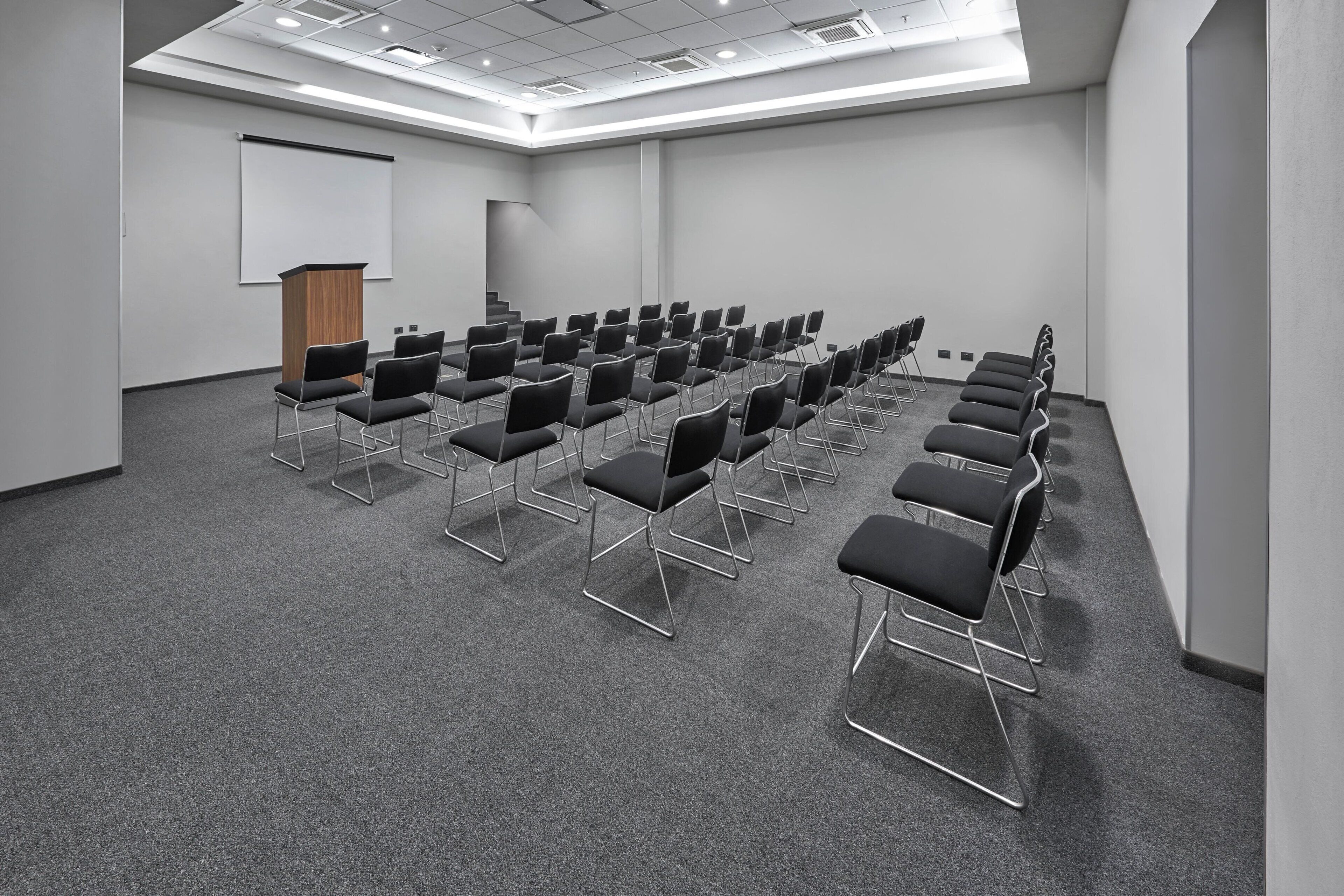 Uma sala de conferências com fileiras de cadeiras, um púlpito e uma tela de projeção.