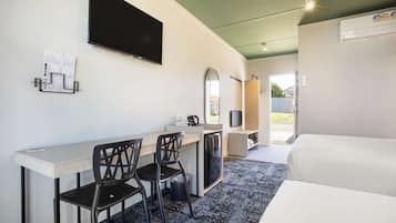 Quarto de hotel com uma cama, uma escrivaninha com duas cadeiras, uma televisão de tela plana, um espelho e uma porta que dá para uma varanda.