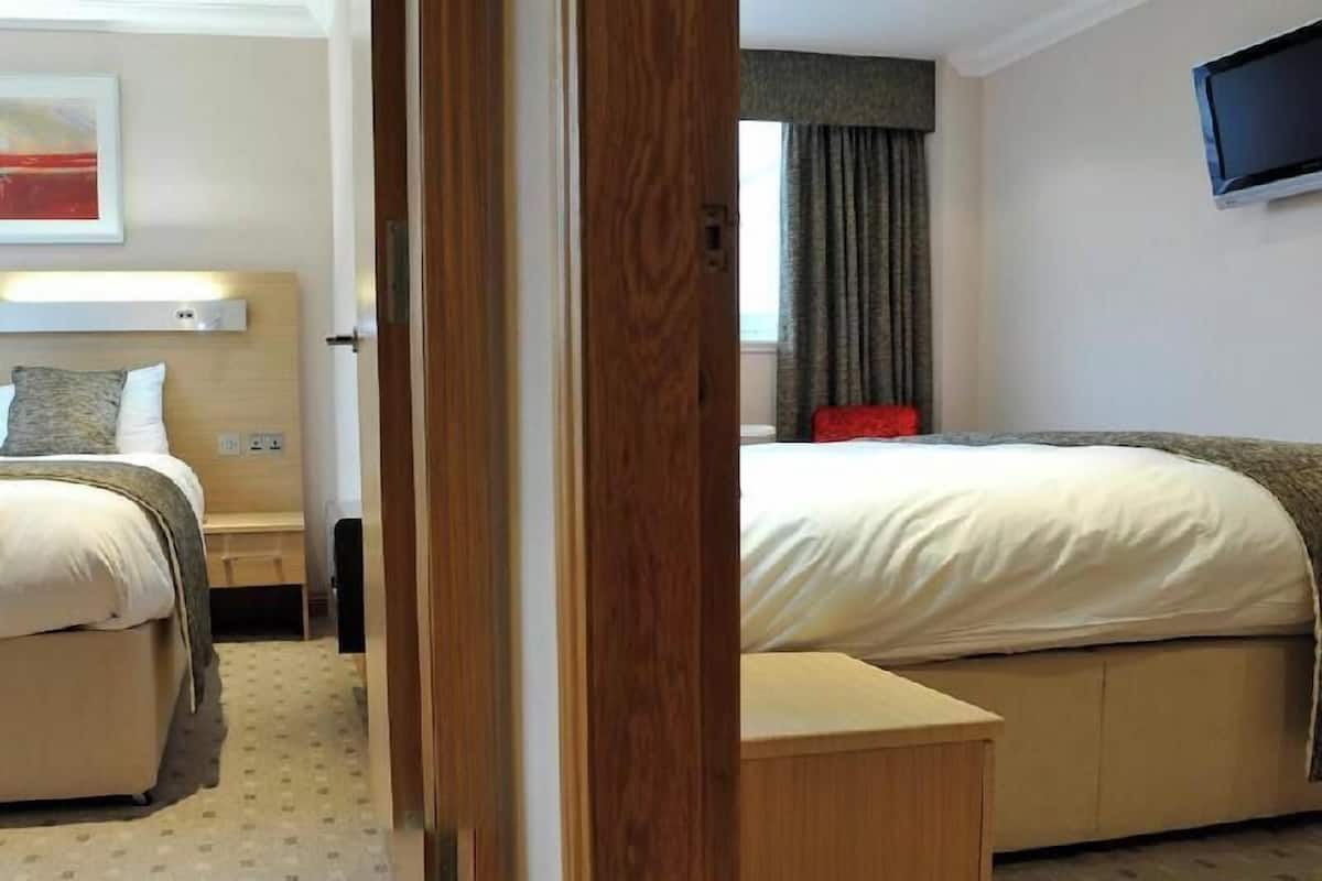 Quarto de hotel com uma cama, mesa de cabeceira, televisão na parede e janela com cortinas.
