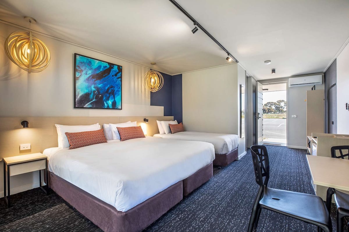 Quarto de hotel moderno com duas camas, uma escrivaninha e uma cadeira.
