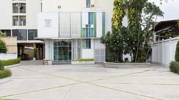 Um edifício moderno com entrada de vidro, rodeado por um espaço ajardinado com pátio pavimentado.
