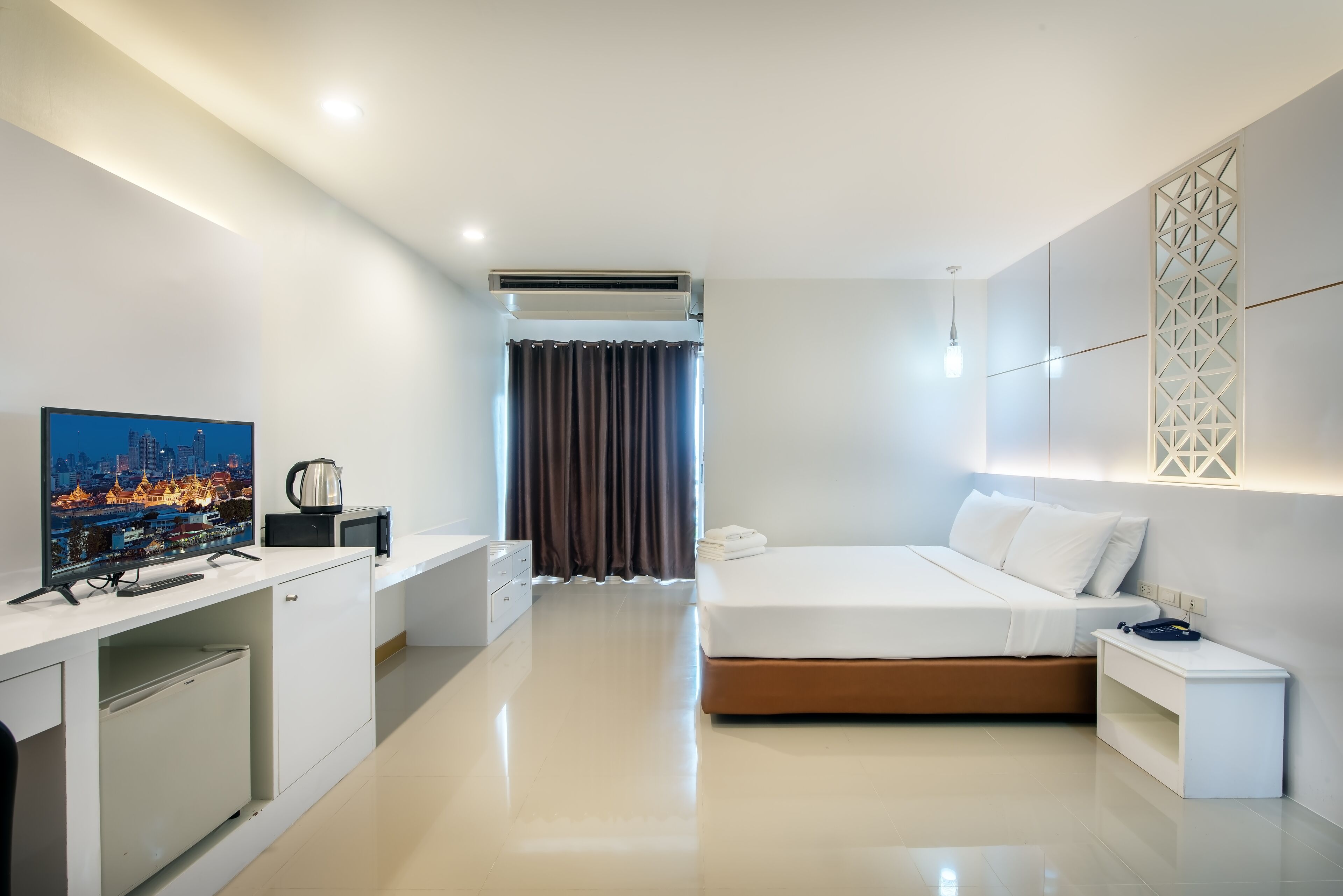 Quarto de hotel moderno com cama, escrivaninha com computador, televisão e aparelho de ar condicionado.