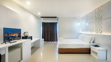 Quarto de hotel moderno com cama, escrivaninha com computador, televisão e aparelho de ar condicionado.