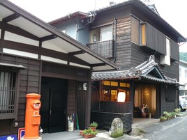 Um edifício tradicional japonês com fachada de madeira escura, telhado telhado e pequena área de entrada com plantas em vasos.