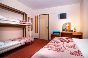 Quarto de hotel com beliche, escrivaninha com laptop, espelho e televisão.