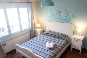 Quarto com cama, duas mesas de cabeceira com luminárias, uma janela e uma parede com desenho de montanha.