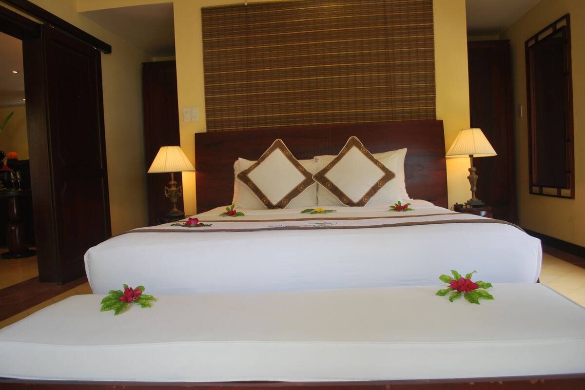 Quarto de hotel com uma cama grande, duas luminárias de cabeceira e uma cabeceira de madeira.