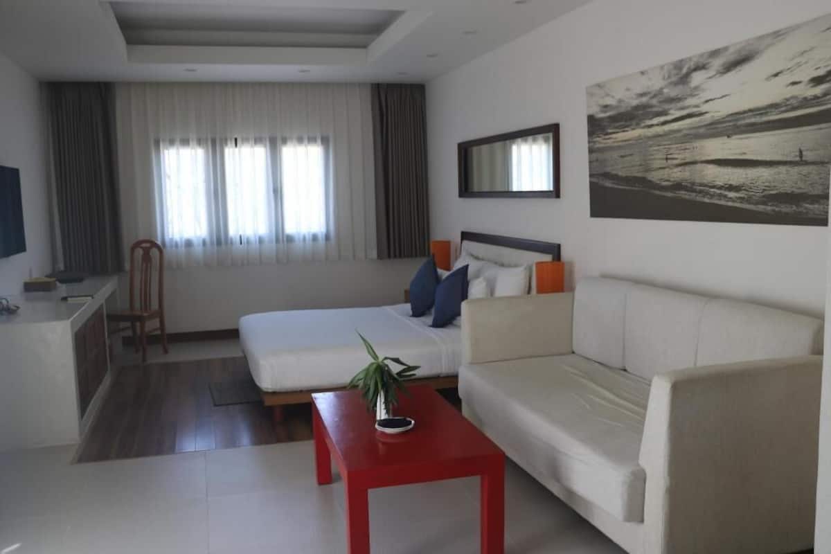Quarto de hotel moderno com uma cama, um sofá, uma mesa vermelha, uma TV e uma grande pintura na parede.