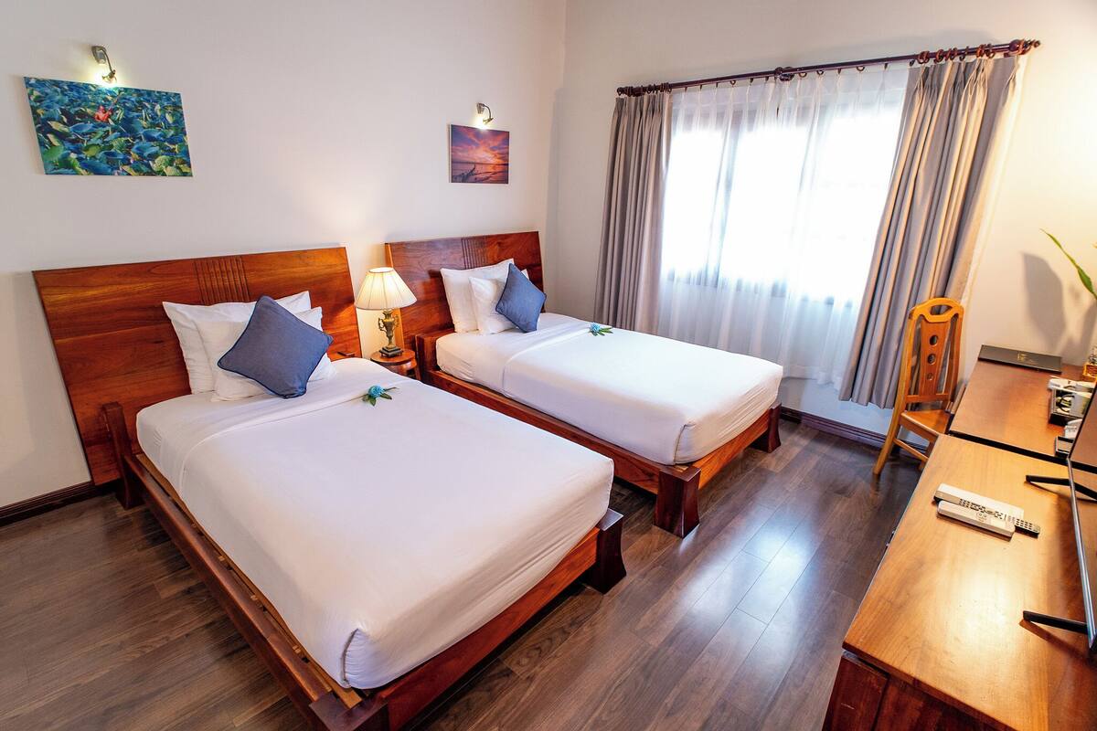 Quarto de hotel com duas camas de madeira, uma escrivaninha e uma cadeira.
