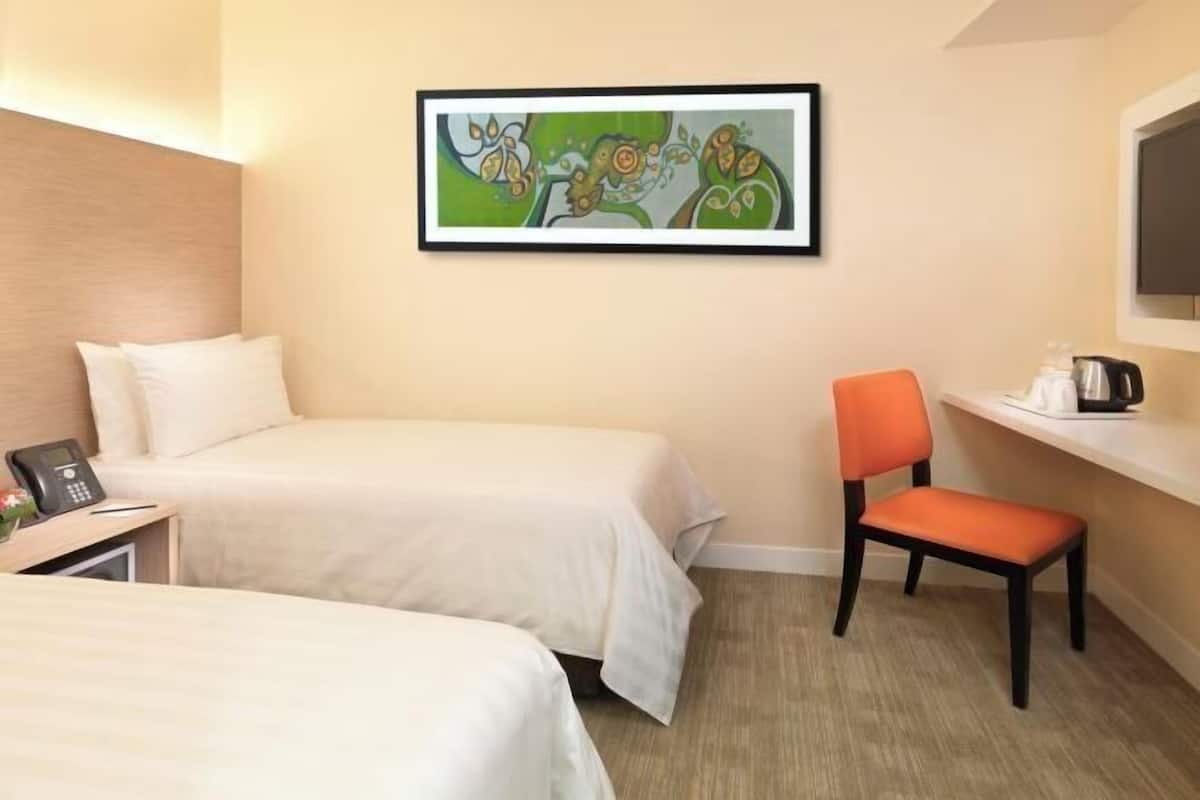 Quarto de hotel com duas camas, uma mesa com telefone, uma cadeira laranja, uma televisão de tela plana e uma pintura abstrata emoldurada na parede.