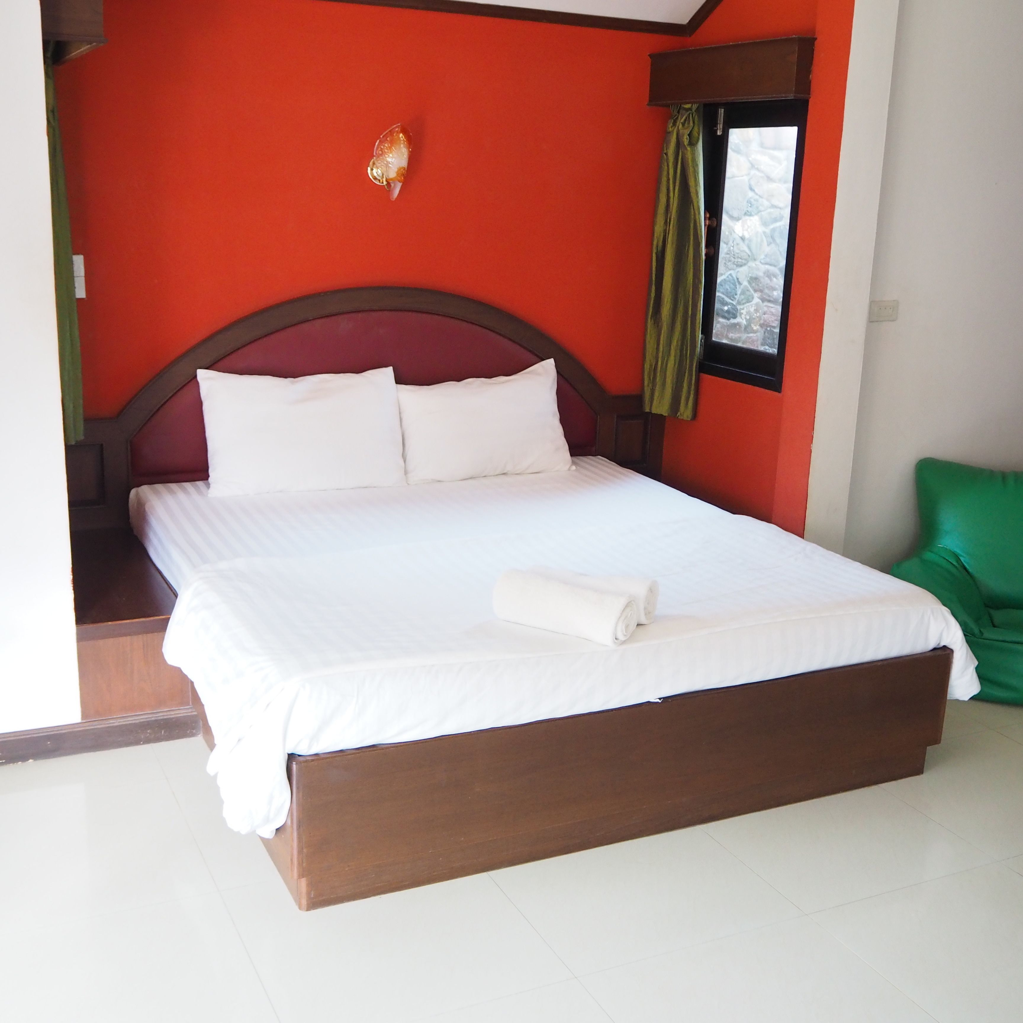 Cama com lençóis brancos, cabeceira de madeira e uma cadeira verde.