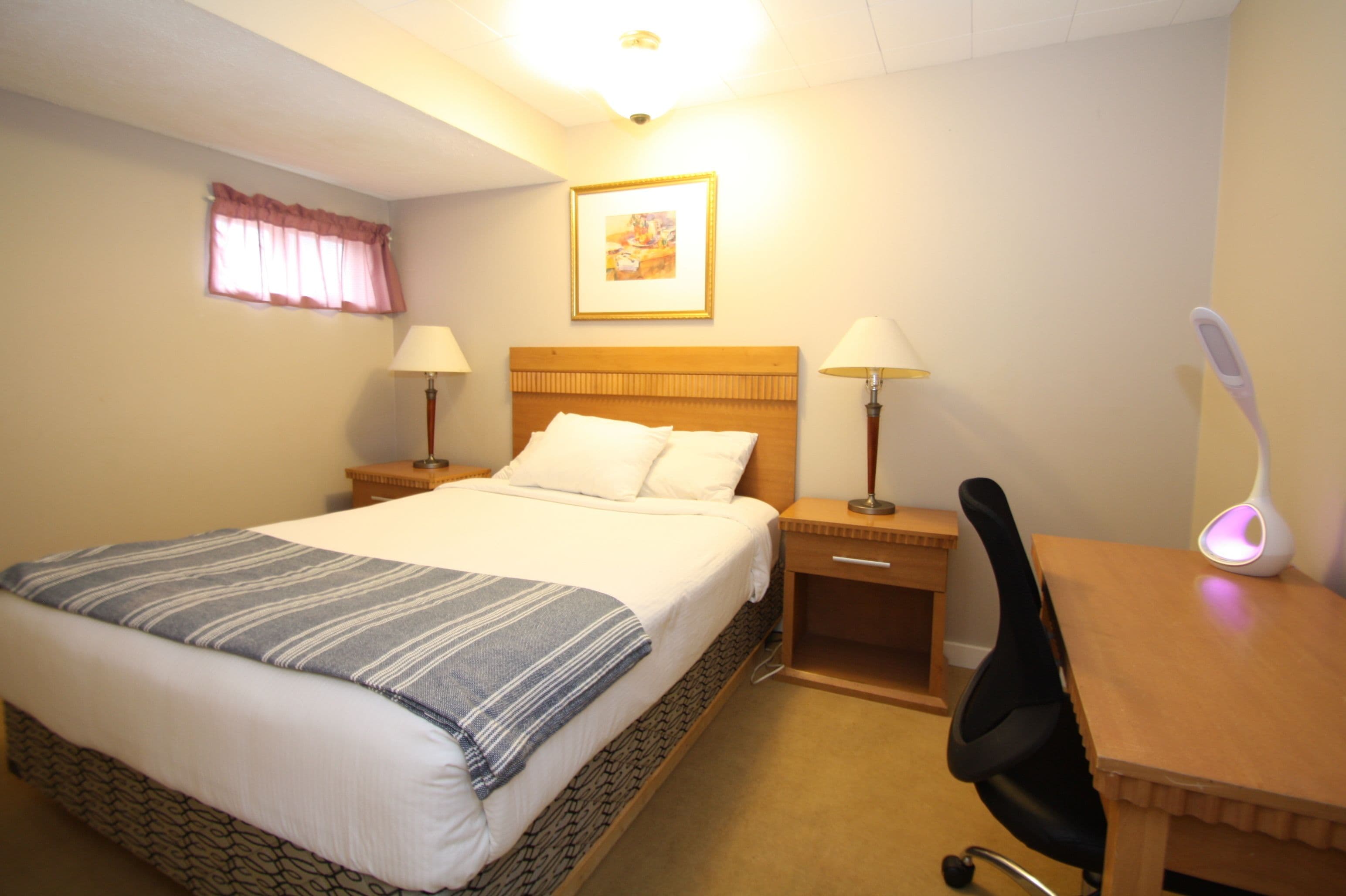 Quarto de hotel com cama, mesas de cabeceira, luminárias, escrivaninha e uma cadeira.