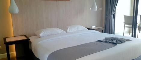 Quarto de hotel moderno com uma cama grande, uma parede de destaque em madeira e vista para o exterior.